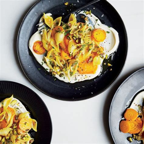 Three Black Plates Topped With Pasta And Veggies On Top Of A White Table