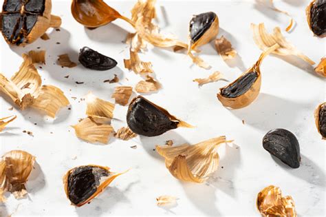 흰색 배경에 누워있는 검은 마늘의 정향 발효 마늘의 껍질과 정향은 무작위로 테이블에 흩어져 있습니다 발효식품 건강식품 비건