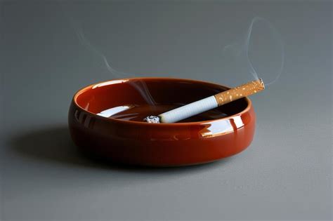 A Half Smoked Cigarette Resting In A Brown Ashtray With Smoke Rising