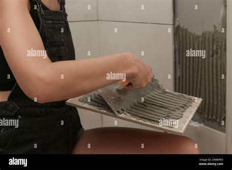 Woman Tiling Bathroom Walls Applying Adhesive On A Tile And Placing
