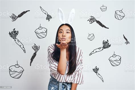 잡을 의 가까이 귀여운 젊은 아시아 여자에 토끼 귀와 캐주얼에 키스를 불어 회색 배경에 서 손으로 그린 당근과 컵 케이크 관능에