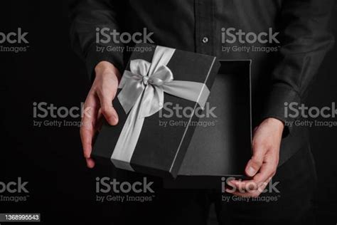 검은 색 배경에 검은 셔츠를 입은 남자가 은색 리본이 달린 열린 선물 상자를 들고 있다 남자에 대한 스톡 사진 및 기타 이미지