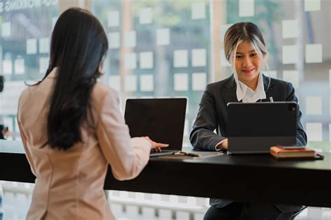 두 명의 아시아 여성 회계사가 노트북 컴퓨터와 금융 문서를 테이블에 올려 놓고 사무실에서 일합니다 2명에 대한 스톡 사진 및