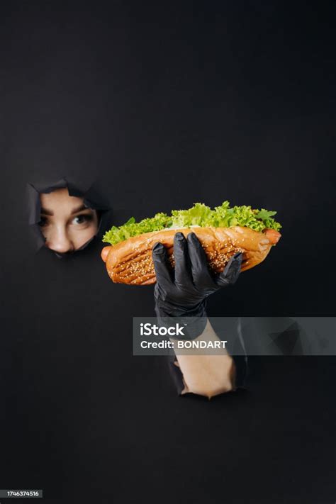 핫도그를 들고 검은 종이 배경에 구멍을 뚫고 있는 여성의 손 길거리 음식 개념 핫도그에 대한 스톡 사진 및 기타 이미지