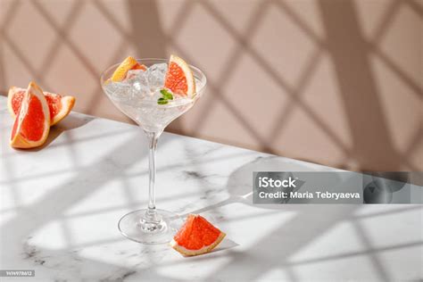 상쾌한 토닉 칵테일 얼음을 곁들인 신선한 차가운 음료 감귤류 슬라이스로 장식 된 신선한 자몽 주스 민트 베이지색과 대리석 배경과 창 그림자 맑은 햇살 햇빛 식전 반주에 대한