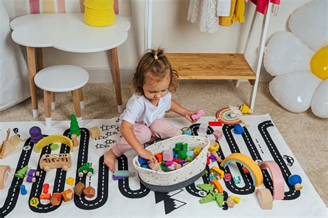 바닥에 앉아있는 어린 소녀는 놀이방에있는 도로 그림이있는 양탄자에 장난감 나무 블록을 가지고 놀고 있습니다 현대 보육원에서 아기와 유아를위한 교육 게임 2 3 살에 대한