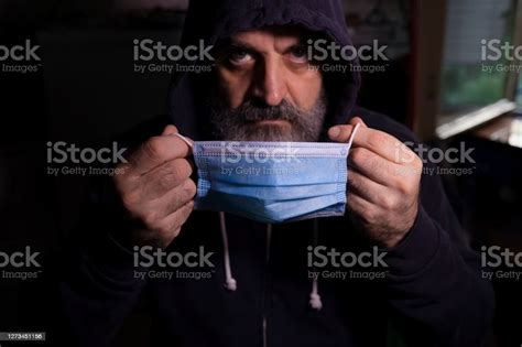 얼굴 앞에서 파란색 외과 마스크를 들고 어두운 후드를 입은 수염난 남자 화가 나서 남자에 대한 스톡 사진 및 기타 이미지
