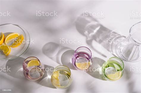 흰색 배경에 접시에 신선한 물과 레몬 조각 밝은 색상 유리 컵 생활 스타일 사진 여름 건강 음료 개념 자연 채광과 하드 섀도우 유리잔에 대한 스톡 사진 및 기타 이미지