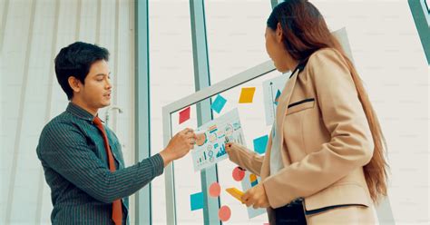 비즈니스 사람들은 사무실의 프로젝트 계획 보드에서 일하고 동료 친구와 대화하여 프로젝트 개발을 분석합니다 그들은 유리 벽에 게시 된 스티커 메모를 사용하여 정리합니다