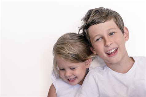 A Laughing Brother And A Shy Sister Stand In White Clothes Against A