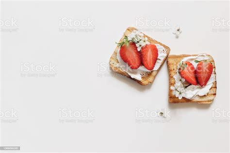 흰색 테이블 배경에 고립 된 코티지 치즈와 딸기를 곁들인 구운 빵 샌드위치 두 개 신선한 과일과 꽃을 곁들인 토스트 건강한 아침