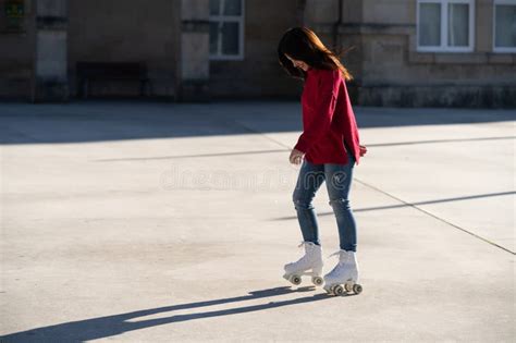 Young Woman Roller Skating Downtown Wearing Red Sweater And Jeans