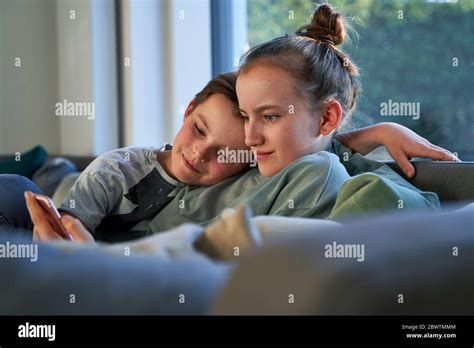 Brother And Sister Sitting On Couch At Home Using Smartphone Stock
