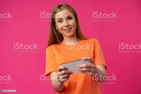 행복한 매력적인 여자는 분홍색 배경에 스마트 폰에 비디오 게임을 재생 Brand Name Smart Phone에 대한 스톡 사진