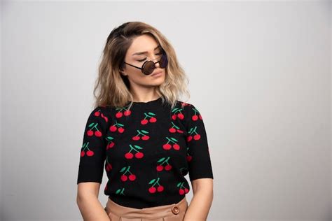 Блондинка в очках стоя на серой стене Бесплатно Фото