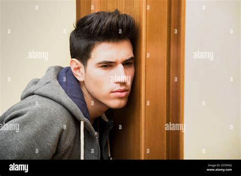 Young Man Listening In Behind A Door With A Concentrated Expression Trying To Overhear Things