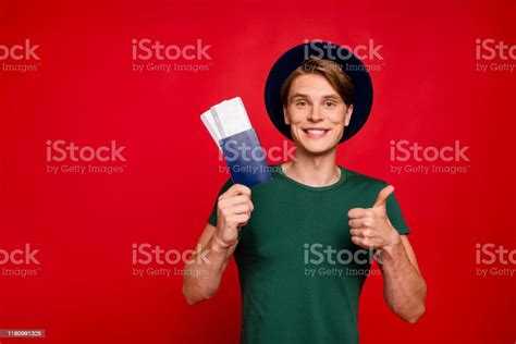 초상화 의 긍정적 인 갈색 머리 남자 여행자 관광 개최 여권 티켓 표시 엄지 손가락 까지 기호 추천 좋은 투어 해외 착용 블루 벨벳 모자 녹색 티셔츠 고립 된 붉은 색 배경