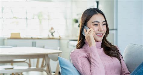 아시아의 아름다운 여자는 소파에 앉아 집에서 휴대폰으로 이야기한다 행복하고 매력적인 어린 소녀는 집에서 여가 시간을 보내고 휴식을 취하고 거실에서 스마트 폰으로 의사