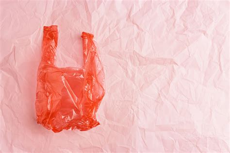 분홍색 구겨진 종이 배경에 빨간 비닐 봉지 빈 공간 의식적인 라이프스타일 개념 최소한의 미적 이미지 일회용 플라스틱 금지 일회용 플라스틱을 줄이기 위한 에코 트렌드 평면도