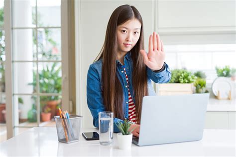 심각하고 자신감있는 표정 방어 제스처와 정지 기호를하고 열린 손으로 컴퓨터 노트북을 사용하여 작업 아름다운 아시아 여성 가정 생활에 대한 스톡 사진 및 기타 이미지 Istock