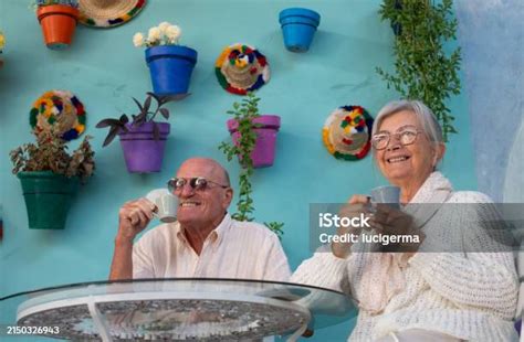 형형색색의 화분이 있는 꽃이 만발한 파티오에 앉아 에스프레소 커피 한 잔과 함께 휴식을 취하는 쾌활한 노인 가족 커플 2명에 대한 스톡 사진 및 기타 이미지 Istock