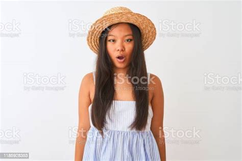 줄무늬 드레스와 모자를 쓰고 고립 된 흰색 배경 위에 서있는 젊은 중국 여성은 놀라움의 표정 두려움 흥분된 얼굴로 충격을 받았습니다 감정에 대한 스톡 사진 및 기타 이미지