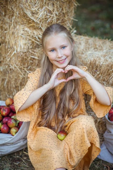 Nice Smiling Girl With Blue Eyes And Blonde Hair Shows A Heart With Her