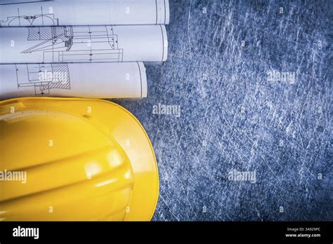 Set Of White Rolled Up Blueprints And Construction Helmet On Metallic Scratched Background