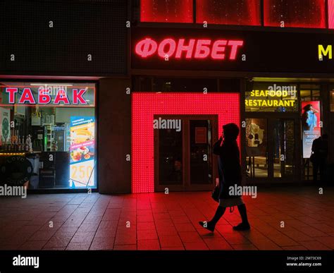 Woman Walking Along The Sidewalk Passes By Shops Windows Illuminated