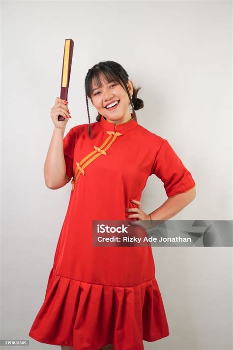 빨간 중국 전통 의상을 입은 젊은 아시아 여성이 큰 노란색 부채를 들고 흰색 배경 위에 고립 된 그녀 옆의 복사 공간을 가리키고 있습니다 음력 설날 파티에 대 한 개념 12