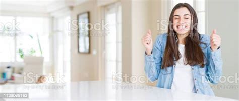 집에서 흰색 테이블에 앉아 아름 다운 젊은 여자의 넓은 각도 그림은 승리 미소를 축 하 상승 팔과 성공에 대 한 흥분 승자 개념입니다 가정 생활에 대한 스톡 사진 및 기타