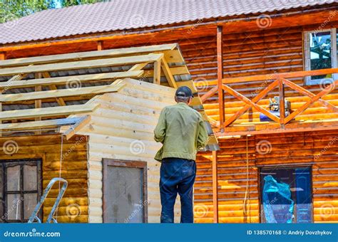 Worker Carpenter And Builder Making A House From The Frame Of A Wooden