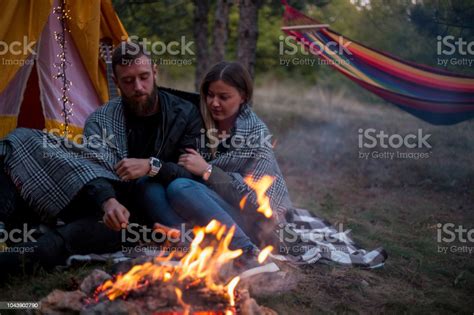 아름 다운 커플 앉아 캠프 파이어 주위에 캠핑 텐트와 배경에 남자 막대기로 화재 제스처 건강한 생활방식에 대한 스톡 사진 및 기타 이미지 Istock