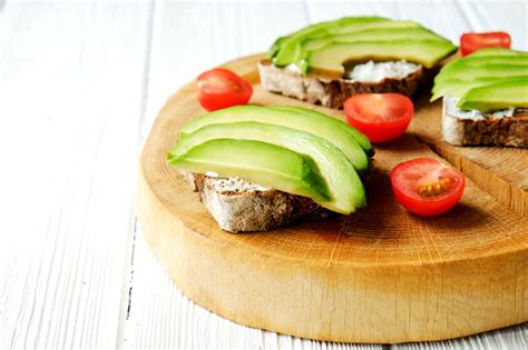 채식 샌드위치 호밀빵 토스트 아보카도 체리 토마토 두꺼운 금이 나무 조각 흰 나무 질감 테이블에 Vegenaise Eggless