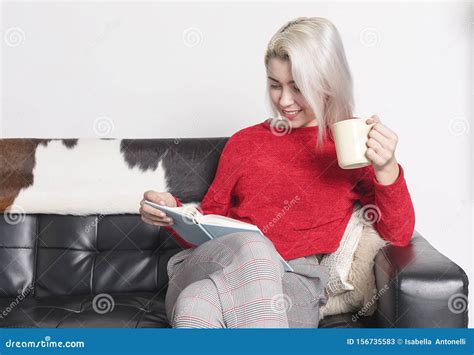 Caucasian Blonde Woman Sitting On Sofa Drinking Coffee And Reading Book