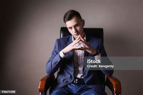 비즈니스 양복과 흰색 셔츠와 그의 손에 유행 시계에 자신감 얼굴로 성공적인 젊은 사업가 검은 가죽의 자에 앉아 있다 세련 된 남자입니다 회사의 이사입니다 감독에 대한 스톡