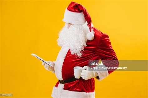 산타 클로스는 손에 뜨거운 커피 한 잔을 들고 서서 주문 목록을 확인합니다 12월에 대한 스톡 사진 및 기타 이미지 12월