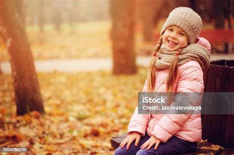 화창한 날에 야외 산책을 즐기는 아이 여자 따뜻한 니트 모자와 스카프 공원에서 벤치에 앉아 미소의 세로 가을에 대한 스톡 사진