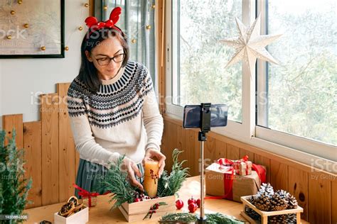 신선한 소나무 가지 촛불 및 크리스마스 장식으로 겨울 이케바나를 만드는 여성 플로리스트 블로거가 스마트 폰 앞에서 스트리밍합니다 중소기업 계절 겨울 워크샵 12월에 대한