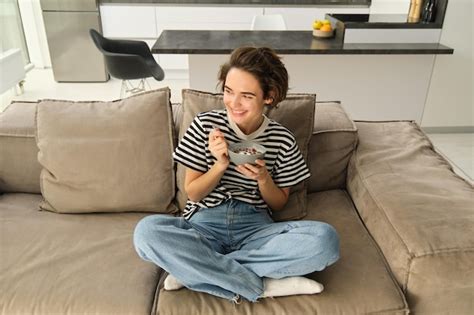 Porträt einer glücklichen brünetten Frau auf dem Sofa sitzt und ihr Frühstück genießt und