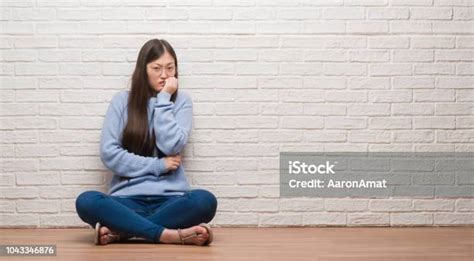 젊은 중국 여자를 강조 하 고 손톱을 물어 뜯고 입에 손을 긴장을 찾고 하는 벽돌 벽을 통해 바닥에 앉아 불안 문제입니다 감정에