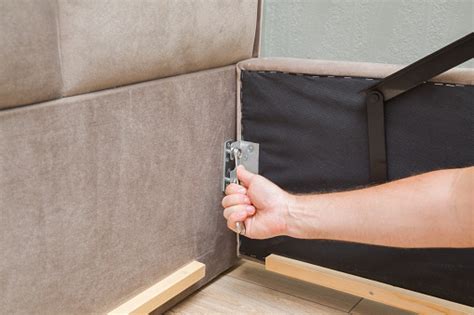 젊은 남자는 렌치와 침대 의 구석에 금속 강철 각도 커넥터에 나사를 사용하여 손 소파의 일부를 함께 넣어 새로운 섬유 가구를