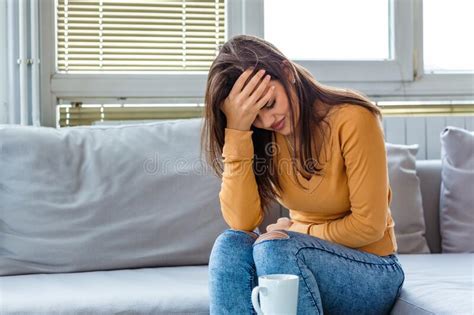 Young Woman Suffering From Abdominal Pain While Sitting On Bed At Home