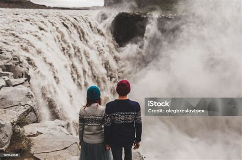 아이슬란드의 유명한 랜드마크 인 데티포스 폭포를 보고 사랑에 빠진 젊은 부부 전통적인 울 스웨터 빨간 머리 모자 회색 스커트 극적인 북유럽 풍경 아이슬란드의 추운 날씨