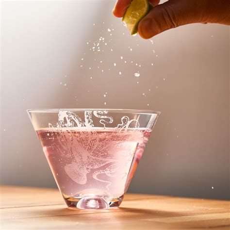 A Hand Squeezes A Lime Over A Pink Liquid In A Lucy Stemless Martini