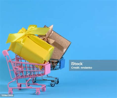 밝은 파란색 배경에 미니어처 금속 트롤리에 실크 활이 있는 노란색 선물 상자 0명에 대한 스톡 사진 및 기타 이미지 0명