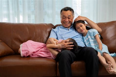 Happy Asian Senior Grandfather Sits On A Couch With His Granddaughter
