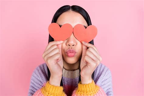 젊고 아름다운 사랑스러운 매력적인 한국 소녀 Pout 입술의 사진은 분홍색 배경에 고립 된 작은 마음으로 눈을 덮습니다 가리기에