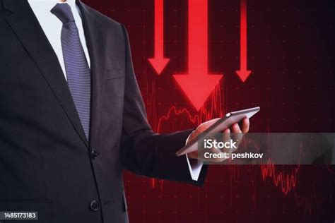 스마트폰을 들고 있는 남성의 손은 아래쪽으로 향하는 빨간색 비즈니스 차트와 흐릿한 배경에 화살표가 있습니다 위기 경기 침체 및 금융 실패 개념 개념에 대한 스톡 사진 및