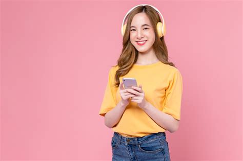 음악을 듣고 헤드폰에 쾌활한 젊은 아시아 여성은 분홍색 배경에 춤과 스마트 폰에 좋아하는 재생 목록 응용 프로그램을 즐길 수